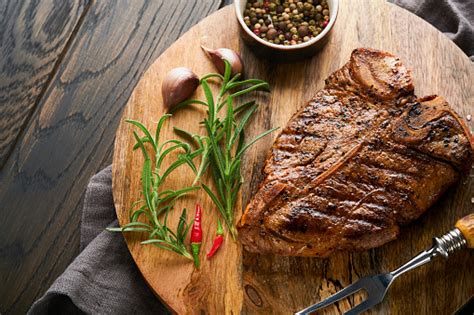 생 스테이크 Tbone 또는 포터 하우스 스테이크 Tbone 또는 포터 하우스는 콘크리트 배경에 검은 세라믹 플레이트에 향신료 소금 및 로즈마리를 곁들인 소스에 담았습니다