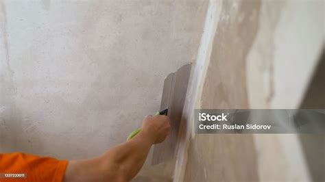 마스터는 벽에 흰색 퍼티를 바르고 낮에 집을 개조하는 방에 퍼티 칼로 얼룩지고 있습니다 작업자는 퍼티 나이프로 벽에 퍼티를 적용합니다 개념에 대한 스톡 사진 및 기타 이미지