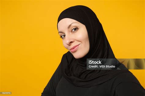 가까이에 젊은 아라비아 무슬림 여자 히 잡 블랙 옷 노란 벽 배경 스튜디오 초상화에 고립 된 휴대 전화에 Selfie 샷을 하 고 사람들 종교적 라이프 스타일 개념입니다