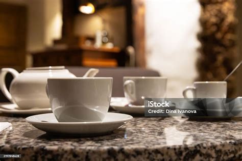 따뜻한 은은한 조명이 들어오는 아늑한 카페 환경에서 화강암 테이블에 찻주전자와 흰색 도자기 컵이 놓인 우아한 차와 커피 아늑한 커피숍 장면 선택적 초점 0명에 대한 스톡
