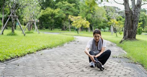 아시아의 매력적인 스포츠 여성은 거리에서 달리는 동안 발목에 통증을 느낀다 운동복을 입은 아름다운 소녀 운동 선수가 공원에서
