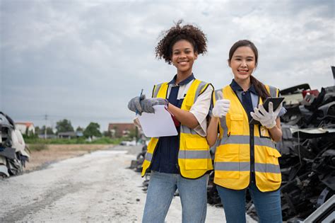 자동차 폐차장에 서서 검사하는 기계 여성 소유자 중소기업 자동차 폐차장에서 예비 부품을 선택하는 더러운 남성 수리공 스크랩 야드 차고에서 재활용을 위해 차량 부품을