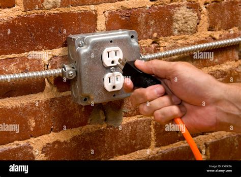 A Mans Hand Plugging In An Extension Cord In A Junction Box Electrical Outlet On A Brick Wall
