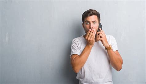 손으로 전화 커버에 말하기 회색 그런 지 벽에 잘생긴 젊은 남자 실수 두려움 침묵 비밀 개념에에서 무서 워의 표현에 대 한