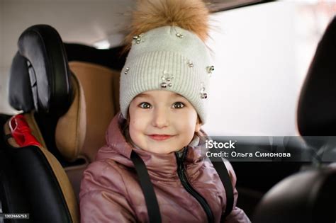 소녀는 안전 벨트를 착용하고 아이의 카시트에 앉아있다 도로 안전 자동차 내부에 있는 어린이의 운송 폼폼이 달린 모자를 쓴 아이가 프레임을 들여다보며 미소를 짓고 있다 아이에