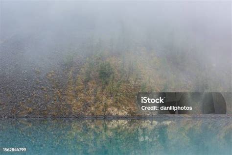 안개 속의 고요한 청록색 호수에서 숲 언덕이 반사되는 단순한 명상 풍경 거울 산 호수에 반영 된 퇴색하는 가을 색상의 전나무가있는 이끼 같은 해안 고산 호수의 가을 해안 0