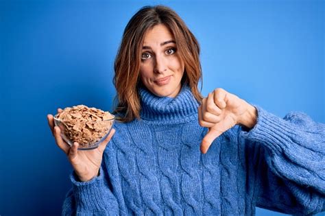 젊은 아름 다운 갈색 머리 여자 들고 그릇 과 건강한 콘플레이크 시리얼 화난 얼굴 부정적인 표시 보여주는 싫어하는 엄지 손가락