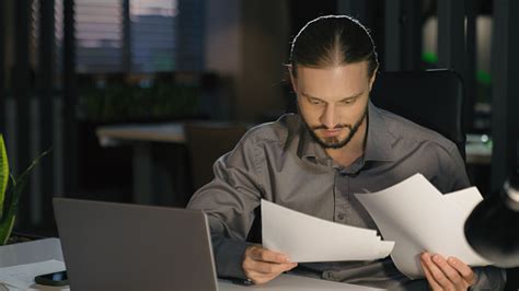 백인 사업가 저녁 사무실 작업 종이 문서 문서 보고서 데이터 정보 입력 휴대용 퍼스널 컴퓨터 서류 작업 만족스러운 사업가 기업가 부기장 확인하는 기업 금융 감독에 대한 스톡