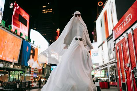 Anonymous Couple In Ghost Costumes Near Illuminated Buildings · Free