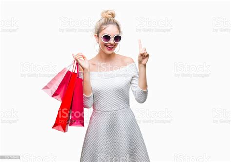 젊은 아름 다운 금발의 여자 고립 된 배경 위에 쇼핑백을 들고 행복 한 얼굴을 가리키는 아이디어 나 질문에 놀라게 번호 하나 가리키기에 대한 스톡 사진 및 기타 이미지