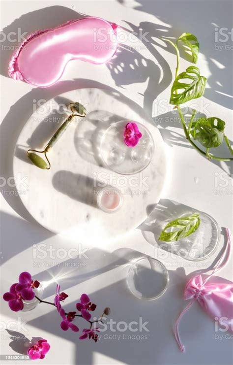 비취 페이스 롤러 대리석 접시에 보습 크림과 핑크 실크 슬립 마스크 몬스터 나뭇잎과 활기찬 마젠타 난초 꽃이국적인 플랫 누워 햇빛 긴 그림자 얼굴 마사지 0명에 대한 스톡