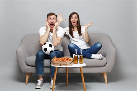 흰색 T 셔츠에 흥분 쾌활 한 부부 여자 남자 축구 팬 응원은 회색 배경에 고립 된 축구 공을 좋아하는 팀 지원 사람들의 감정 스포츠 가족 레저 라이프 스타일 개념입니다