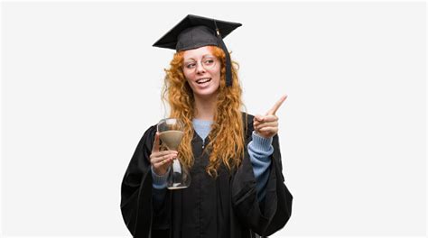 빨강 머리 젊은 학생 여자 입고 졸업 유니폼 들고 모래 시계 옆에 손 및 손가락으로 가리키는 매우 행복 가리키기에 대한 스톡 사진 및 기타 이미지 Istock