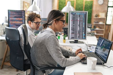 Young Female Programmer Standing On Her Desk Coding On A Laptop Having