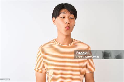 캐주얼 스트라이프 티셔츠를 입은 젊은 중국 남자는 입술 미친 코믹 한 제스처와 물고기 얼굴을 만드는 고립 된 흰색 배경 위에 서 재미있는 표현 기이함에 대한 스톡 사진 및