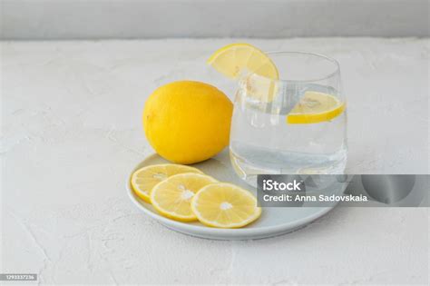 두 개의 레몬 슬라이스가 있는 투명한 물 한 잔 레몬 슬라이스 3개 레몬 통이 흰색 접시 에 놓여 있습니다 감귤류 과일에 대한 스톡 사진 및 기타 이미지 Istock