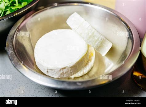 A Whole Wheel Of Brie Cheese Alongside A Sliced Piece On A Metal Bowl