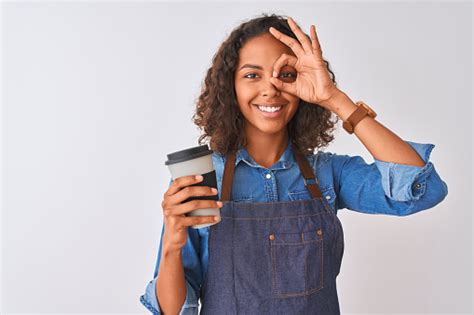 젊은 브라질 바리스타 여자 마시는 손가락을 통해 보고 눈으로 확인 기호를 하 고 행복 한 얼굴 미소와 고립 된 회색 배경 위에 커피를 멀리 눈 신체 부분에 대한 스톡 사진