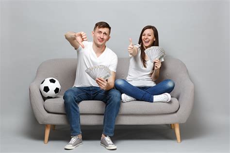 커플 여자 남자 축구 팬 응원 좋아하는 팀 달러 지폐 현금 돈에 돈의 팬을 들고는 회색 배경에 고립 된 위아래로 엄지손가락을 보여주는 스포츠 가족 라이프 스타일 개념입니다