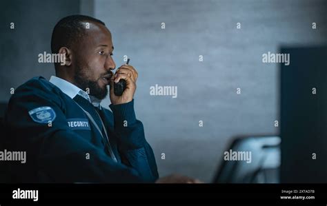 African American Security Officer Or Dispatch In Uniform Uses Tablet Computer And Walkie Talkie