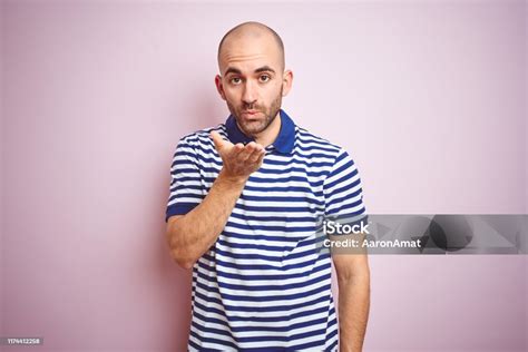 젊은 대머리 남자 와 수염 을 입고 캐주얼 스트라이프 블루 티셔츠 위에 분홍색 고립 된 배경 보고 카메라 불고 키스 와 함께 공기에 사랑스러운 되 고 사랑의 표현 T 셔츠에