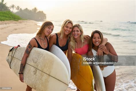 서핑 보드를 가진 4 명의 여성 그룹이 모래 해변에 서 있습니다 수영복을 입은 친구들이 여름 서핑 캠프를 즐깁니다 바다에서 사진을 찍기 위해 미소를 지으며 포즈를 취하고