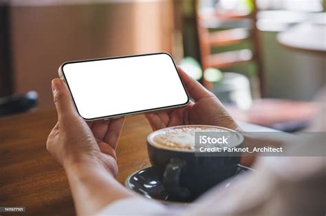 나무 테이블에 커피 컵이있는 빈 데스크톱 화면이있는 휴대 전화를 들고있는 손의 모형 이미지 35 39세에 대한 스톡 사진 및 기타 이미지 35 39세 Brand