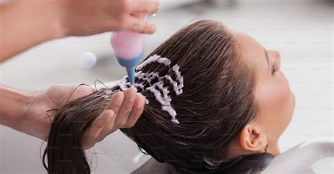 아름다운 여자가 미용실에서 머리를 감고 있다 그녀는 기쁨과 휴식으로 앉아 있습니다 미용사가 샴푸 한 병을 들고 고객의 머리카락에 바르고 있습니다 사진