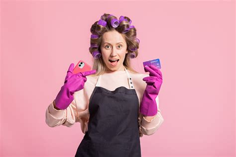 젊은 여성은 신용 카드를 손가락으로 가리키고 손에 전화를 쥐고 청소 장갑을 착용하고 온라인 상점 앱 홈 쇼핑 분홍색 배경의