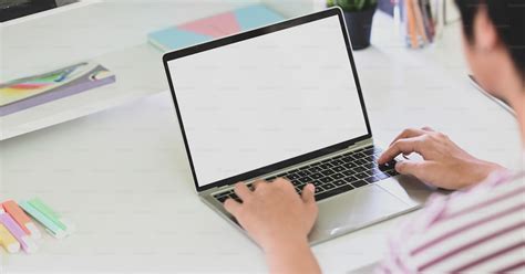 편안한 거실에서 흰색 작업 책상을 놓고 흰색 빈 화면 컴퓨터 노트북에 타이핑하는 창의적인 남자의 비하인드 샷 재택 근무 및