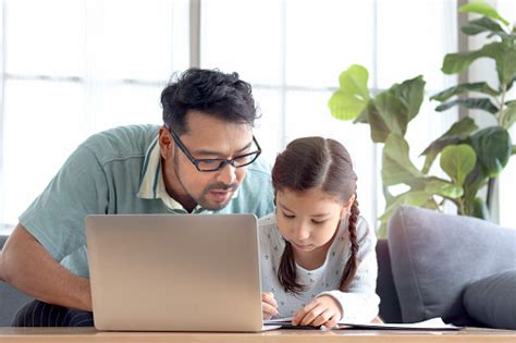 잘 생긴 젊은 아버지는 사랑스러운 소녀 딸에게 학교 숙제를하도록 가르치고 집에서 전자 학습 학습을 위해 노트북 컴퓨터를 사용하고 아빠와 아이는 교육과 인터넷 검색을 위해