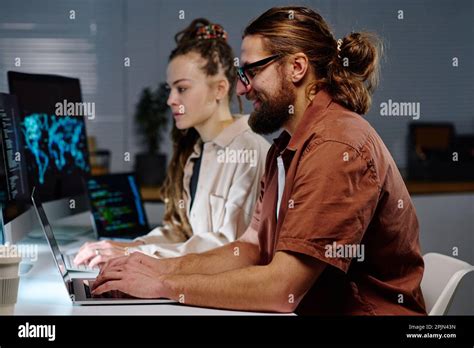 Side View Of Young Male It Engineer Typing On Laptop Keyboard While Decoding Data On Screen