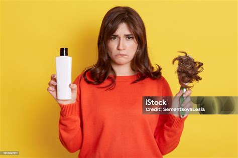 부끄러운 머리와 빗병을 들고 캐주얼 한 옷을 입고 실망 한 여성은 노란 배경에 고립 된 슬픈 표정과 지갑 입술로 카메라를 봅니다 20 24세에 대한 스톡 사진 및 기타