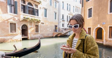 베니스의 아름다운 수로 근처를 걷는 동안 전화를 사용하는 젊은 여성 이탈리아에서 휴가의 개념입니다 코트 선글라스와 화려한 숄을 착용 하 고 백인 세련 된 여자 사진