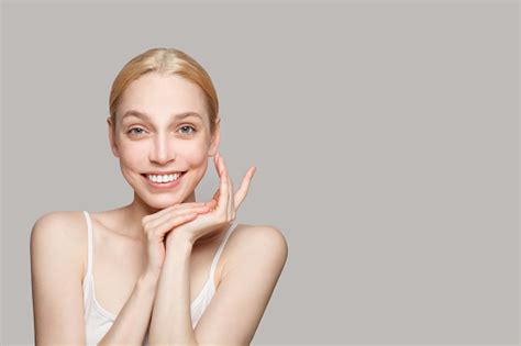 행복한 금발 여자는 회색 배경에 고립된 그녀의 얼굴을 웃고 만지고 있다 미용 화장품 스킨케어 글래머 20 24세에 대한 스톡 사진 및 기타 이미지 Istock