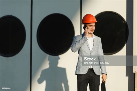 젊은 이루어지지 성공적인 사업가 회색 양복과 보호 건설 오렌지 헬멧 들고 태블릿 휴대 전화 통화 라운드 윈도우 배경 문에 대 한 항구에 서 20 29세에 대한 스톡 사진 및