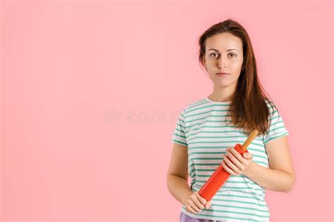 An Irritated Middle Aged Woman Holds A Red Rolling Pin In Her Hands