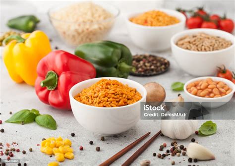 삶은 긴 곡물 바스마티 쌀을 곁들인 흰 그릇 접시에 야채와 버섯을 넣고 지팡이와 옥수수 마늘 바질을 곁들인 파프리카 후추를 곁들인 밝은 테이블 배경에 있습니다 건강한 비건