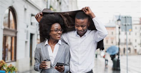 행복한 아프리카 계 미국인 남자와 여자는 도시 거리를 걷는 동안 재킷 아래 비를 피하고 숨어 있습니다 비즈니스 미팅에 참석하는