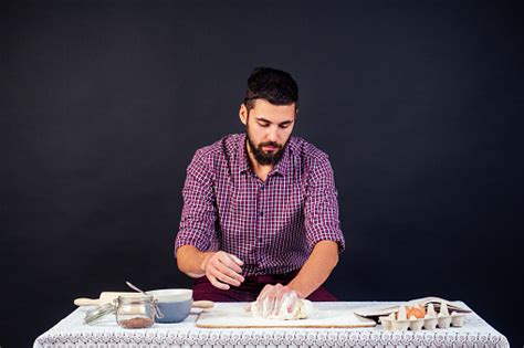 수염을 가진 젊고 매력적인 이탈리아 남자 빵 굽는 사람은 스튜디오의 검은 배경에 밀가루 이탈리아 피자를 뿌린 반죽을 만듭니다 과자는 케이크를 굽는다 25 29세에 대한 스톡