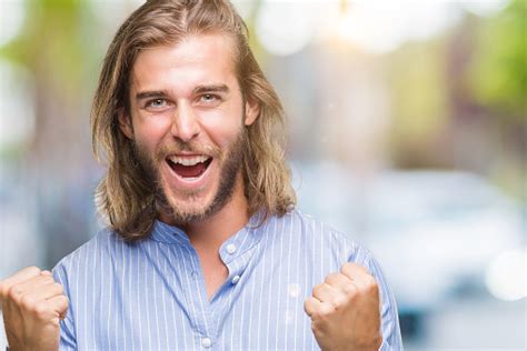 축 하 하는 고립 된 배경 위에 긴 머리를 가진 젊은 잘생긴 남자 놀라게 무기 제기와 성공을 위한 깜짝 놀라게 고 눈을 엽니다 우승자 개념입니다 긍정적인 감정 표현에 대한