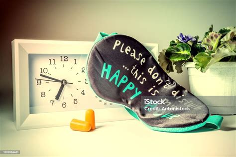 흰색 알람 시계 재미있는 수면 마스크 귀마개와 침실 클로즈업의 침대 근처 의 야간 스탠드에 냄비에 꽃과 현대 시계 오래 된