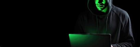 Premium AI Image Hacker Without Face In A Hood Holds A Laptop On A Dark Background Banner