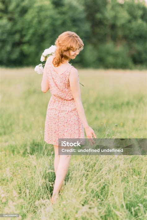 흰색 모란 꽃다발을 들고 일몰에 여름 필드 또는 정원에서 산책 가벼운 드레스에 아름다운 젊은 백인 금발 여성 야외에서 꽃을 가진 여자 개화기에 대한 스톡 사진 및 기타