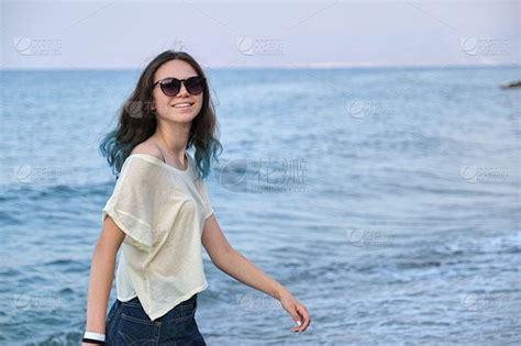蓝色头发戴着墨镜的时髦女孩沿着海滩散步