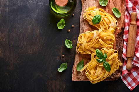 타글리아텔 수제 파스타 바질 잎 밀가루 후추 올리브 오일 체리 토마토 롤링 핀 파스타 나이프를 어두운 오래된 나무 배경에 놓습니다 식품 개념 모의 복사 공간이 있는