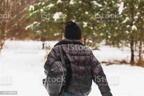 겨울 숲에서 검은 재킷과 모자를 쓴 빨간 머리 곱슬 여자 휴가를 즐기는 예쁜 여자 자연에서 가방을 가진 소녀 행복을 느껴보세요