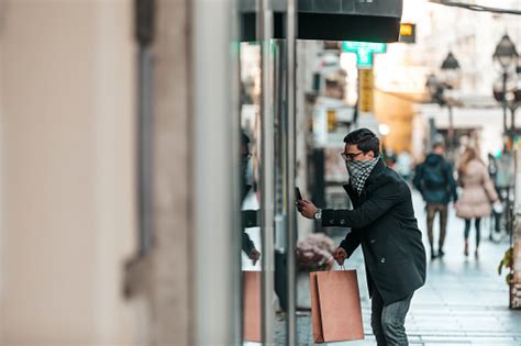 코트와 보호 마스크를 쓴 진지한 청년이 가게 창문 근처에서 색깔의 가방을 들고 있다 고객에 대한 스톡 사진 및 기타 이미지 고객 쇼핑 25 29세 Istock