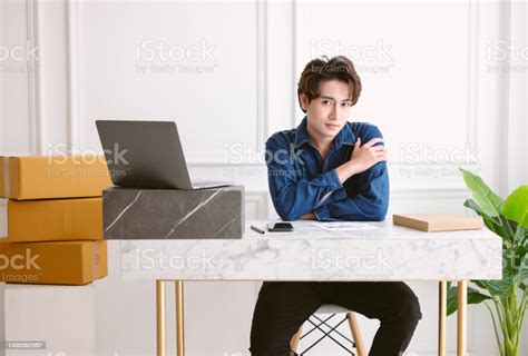 젊은 성공적인 중소 기업 소유자의 초상화 아시아 남자는 홈 오피스에서 상자와 함께 행복한 카메라 작업을 봅니다 중소 기업 기업가