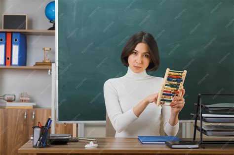 Penser Une Jeune Enseignante Tenant Un Boulier Assis Au Bureau Avec Des Outils Scolaires En